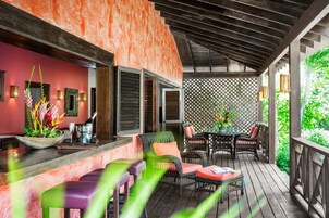 Uma área de estar coberta ao ar livre, com mobiliário de vime, um balcão de bar e um arranjo decorativo de plantas.