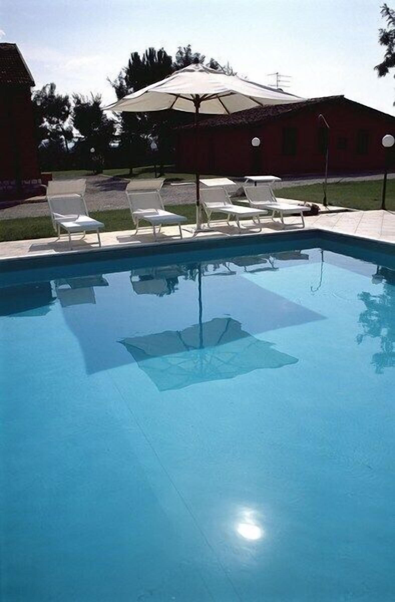 Uma piscina com água azul cristalina, rodeada por espreguiçadeiras brancas e um grande guarda-sol.