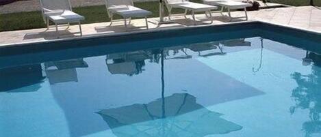 Uma piscina com água azul cristalina, rodeada por espreguiçadeiras brancas e um grande guarda-sol.