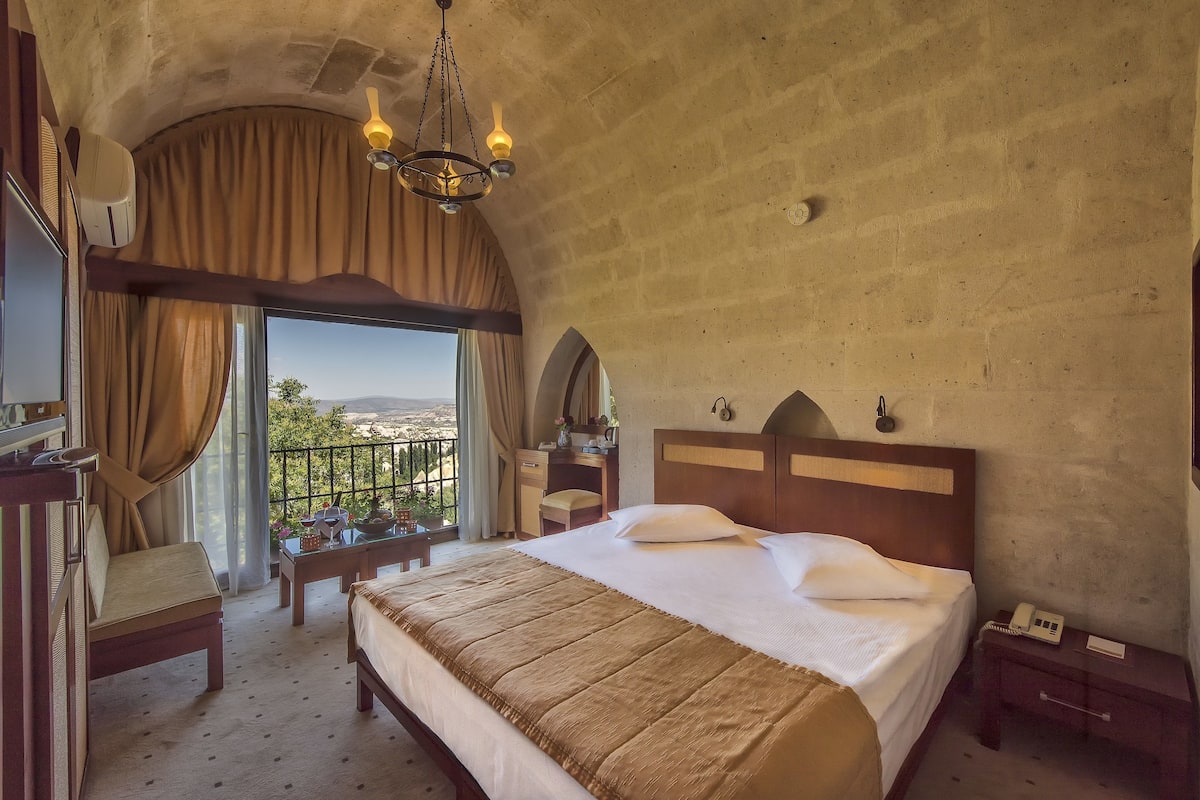 Quarto de hotel com uma cama grande, uma escrivaninha, uma cadeira e vista para o exterior.
