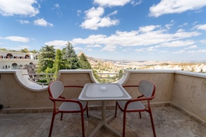 Terraço com duas cadeiras e uma mesa, com vista para uma paisagem montanhosa sob um céu claro.