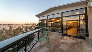 Varanda de hotel com vista para a paisagem, área de estar com cadeiras e porta de vidro que dá para o interior.