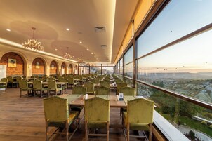 Uma ampla área de refeições com mesas e cadeiras altas, grandes janelas com vista para a cidade e um lustre moderno.