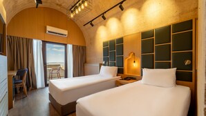 Quarto de hotel com duas camas, uma escrivaninha e vista para a praia.