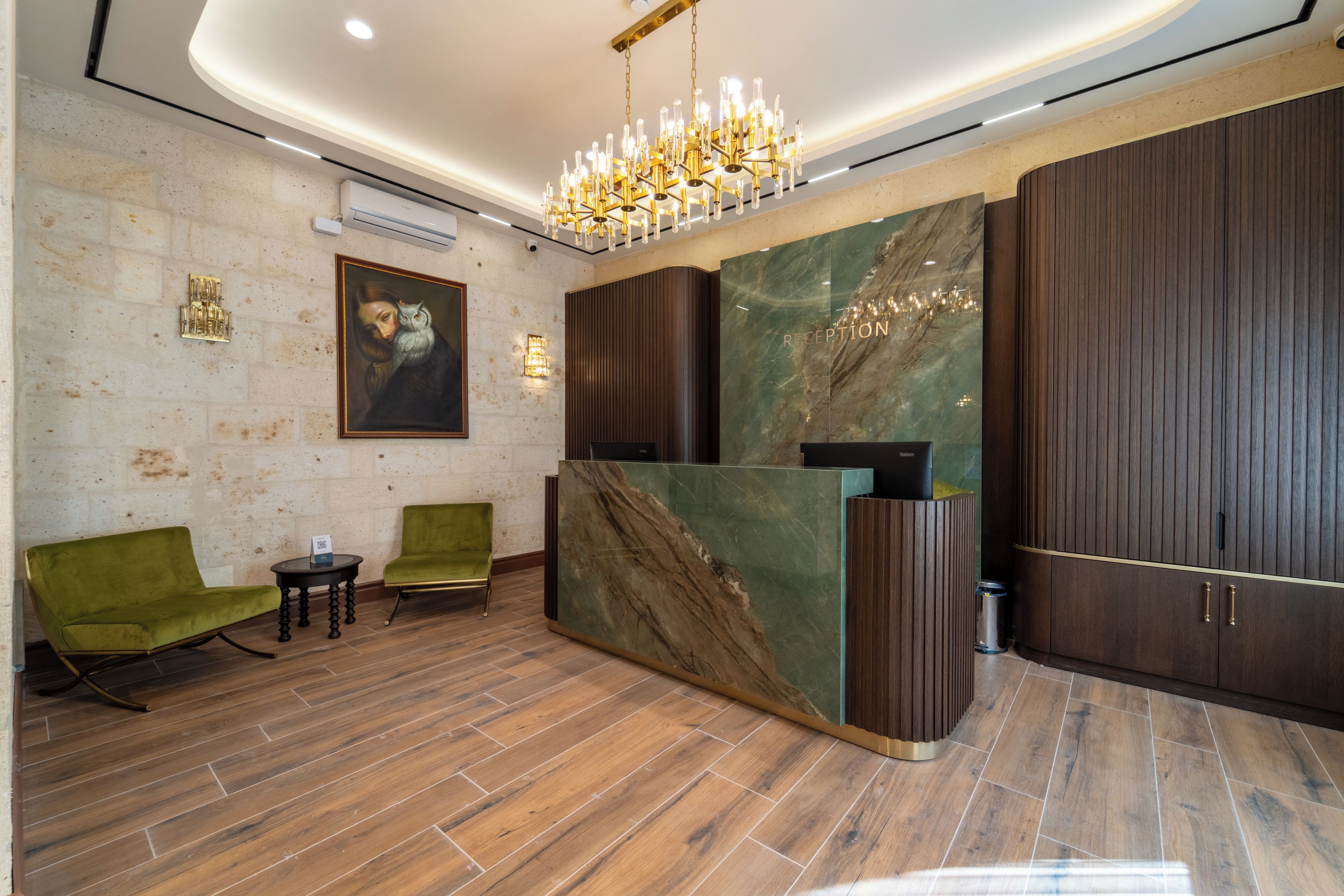 Uma área de recepção com um balcão de mármore, cadeiras verdes, um candelabro e um quadro na parede.