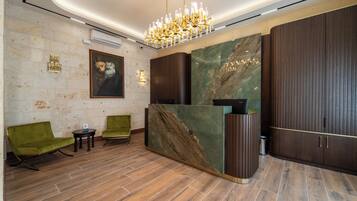 Uma área de recepção com um balcão de mármore, cadeiras verdes, um candelabro e um quadro na parede.