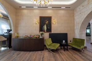 Uma área de recepção com balcão de madeira, duas poltronas verdes, um quadro na parede e um lustre.
