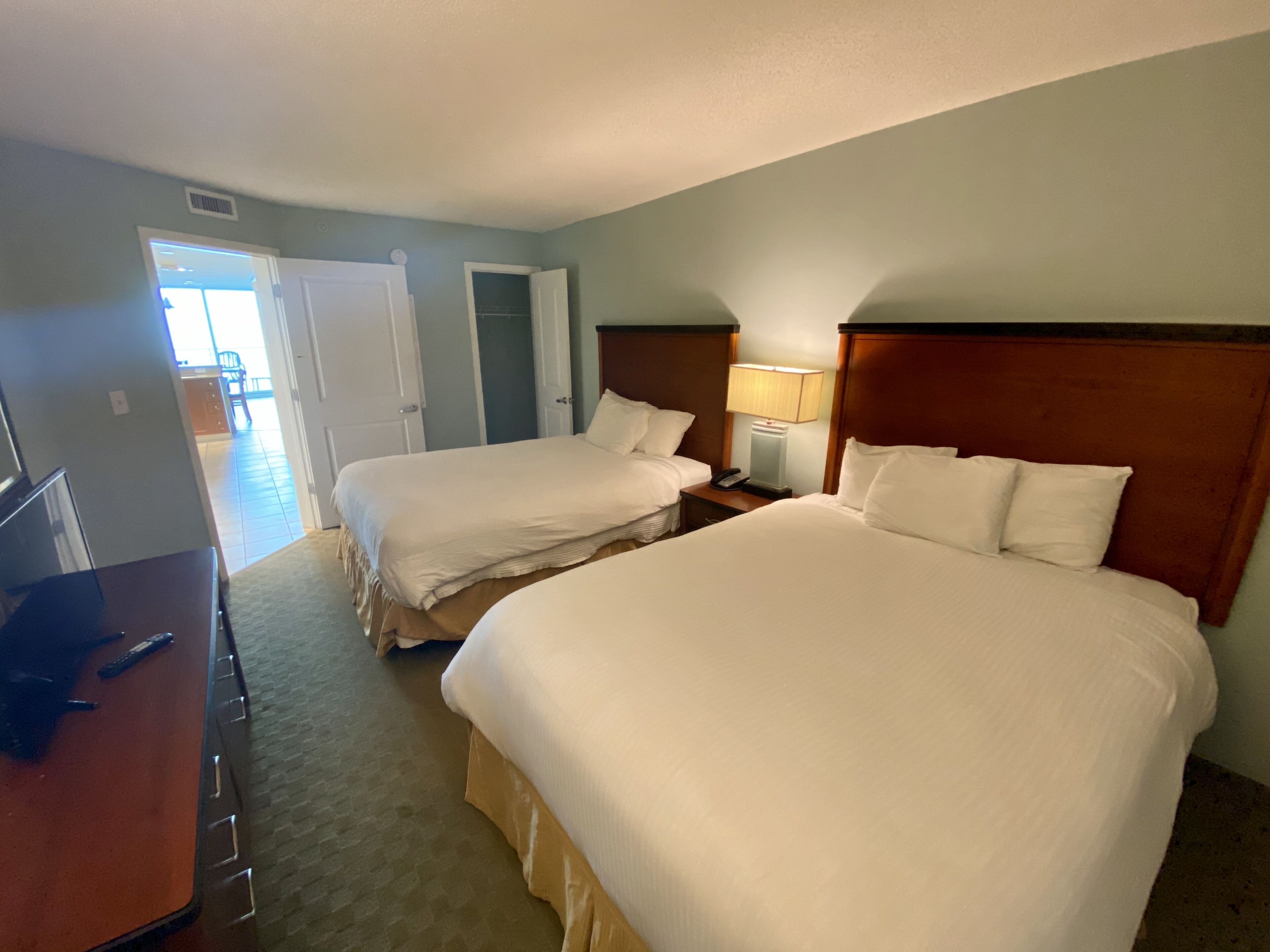 Quarto de hotel com duas camas, uma escrivaninha com computador e porta para uma varanda.