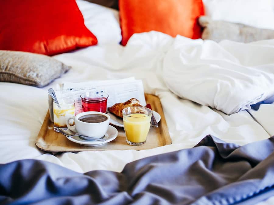 Uma bandeja de café da manhã sobre a cama, com um jornal, uma xícara de café, um copo de suco de laranja e um croissant.