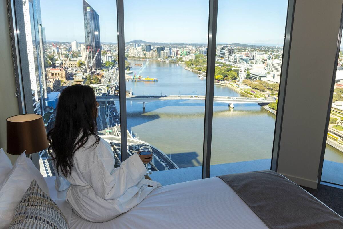 Quarto de hotel com uma janela grande que oferece vista para a paisagem urbana, incluindo um rio e pontes.
