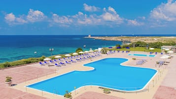 Piscina com cadeiras de praia e guarda-sóis, céu azul límpido e vista para o mar.