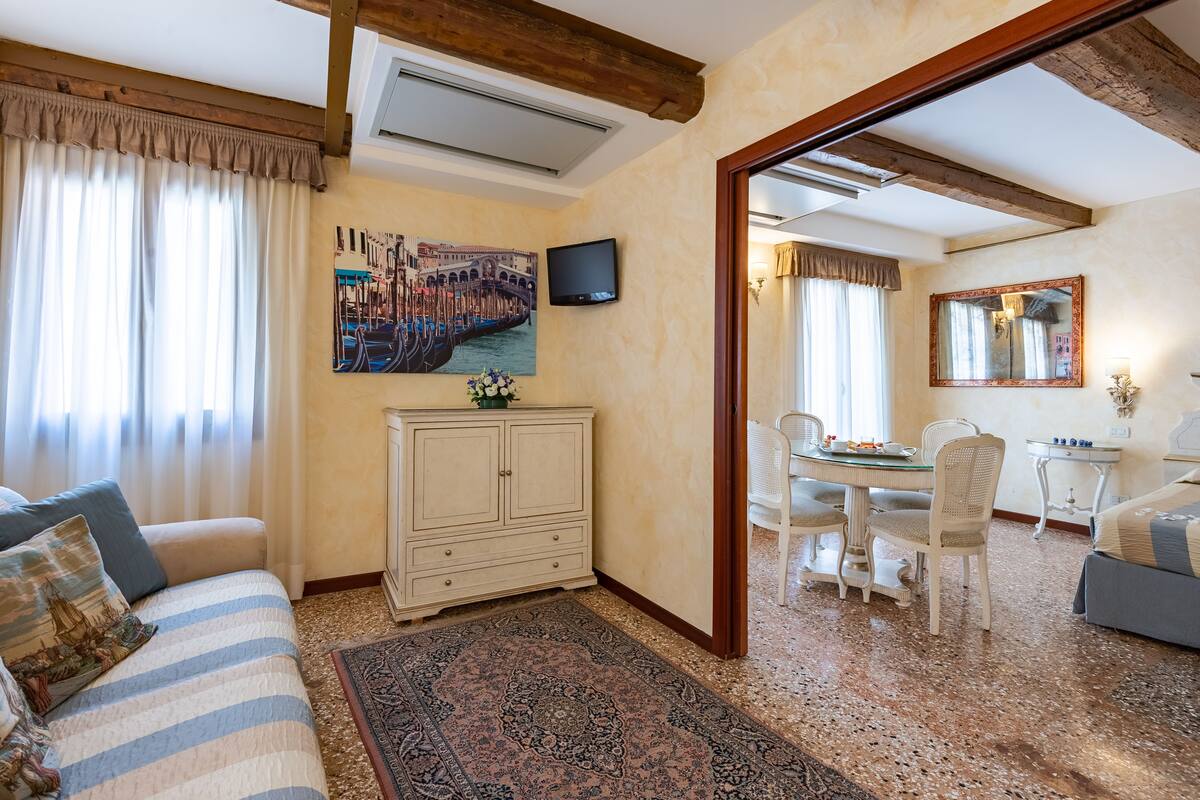 Um quarto aconchegante com um sofá listrado, uma mesa de jantar com cadeiras, um armário e um quadro de uma ponte.