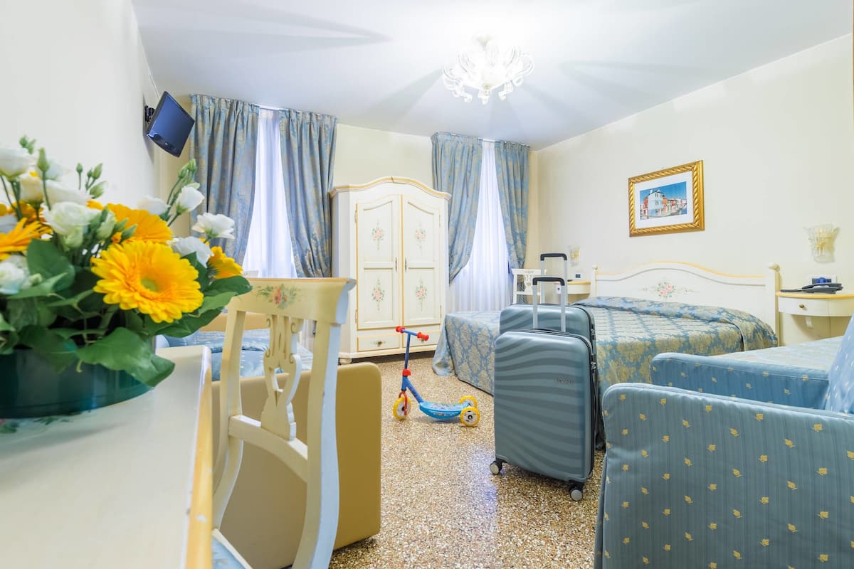 Quarto de hotel com cama, escrivaninha, cadeira, guarda-roupa, mesinha e televisão.