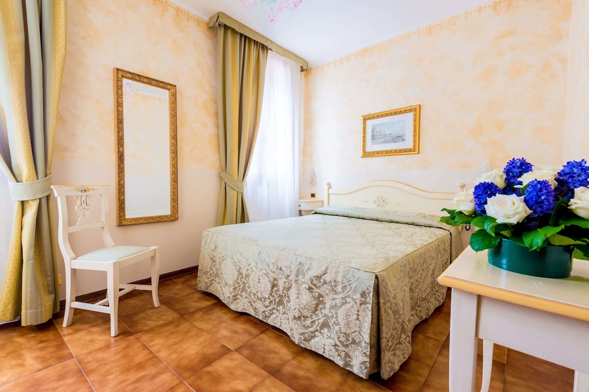 Quarto com uma cama, uma cadeira, uma mesa com um vaso de flores e um quadro na parede.