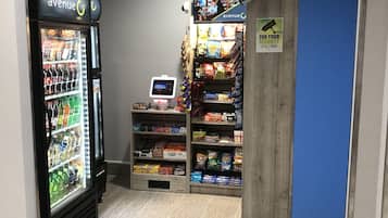 Uma área de máquinas de venda automática com um refrigerador e prateleiras repletas de lanches e bebidas.