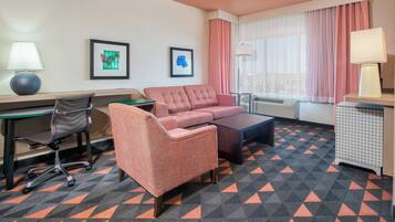 Quarto de hotel com sofá, poltrona, escrivaninha e carpete estampado.