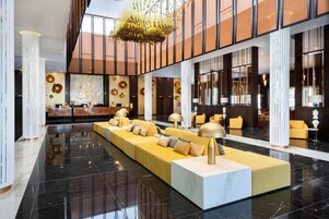 Um hall amplo com um extenso sofá amarelo, piso de mármore e um lustre moderno.