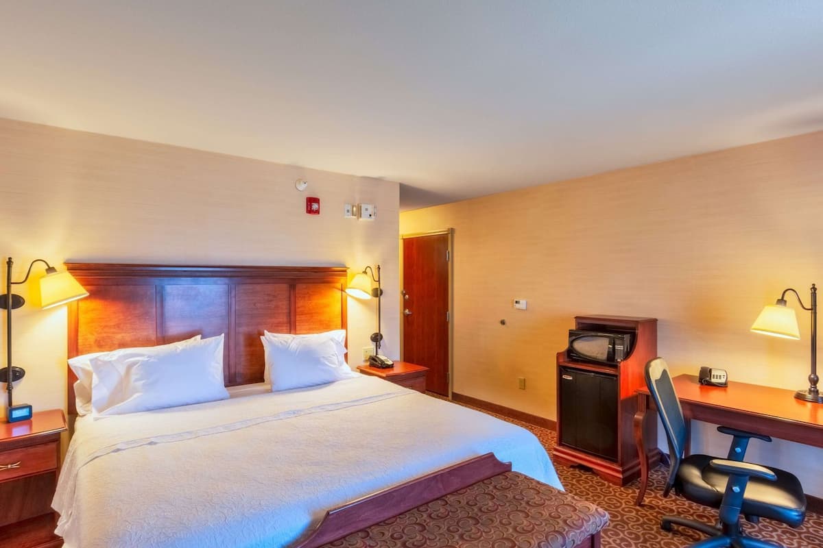 Quarto de hotel com cama, abajures, escrivaninha com cadeira, televisão e guarda-roupa.