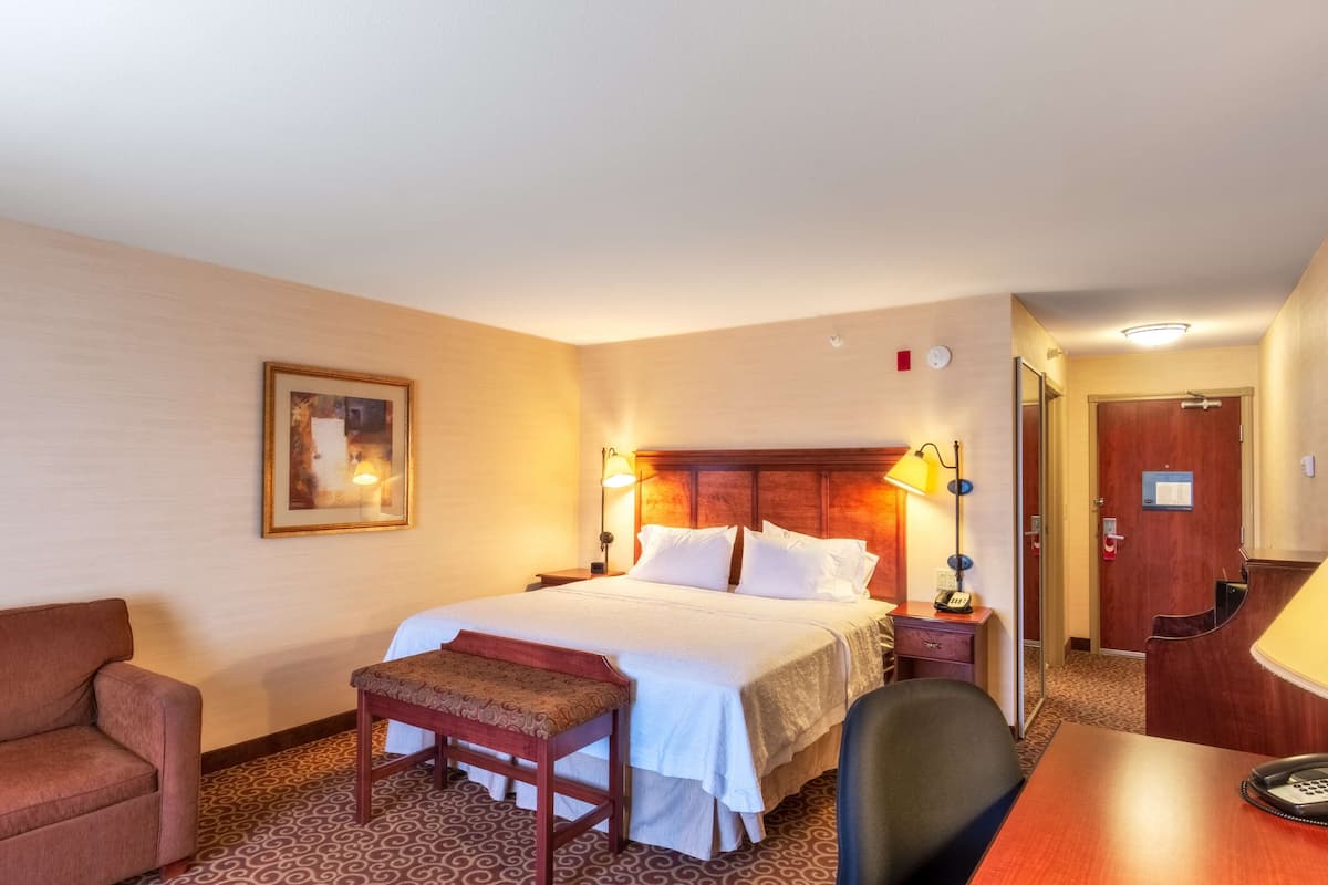 Quarto de hotel com cama, escrivaninha, cadeira, abajur e quadro na parede.