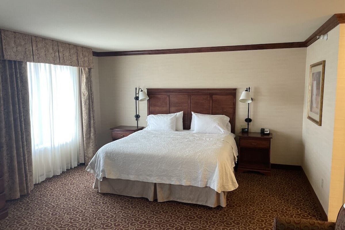 Quarto de hotel com uma cama grande, duas mesas de cabeceira, uma cabeceira, uma janela com cortinas e um tapete estampado.