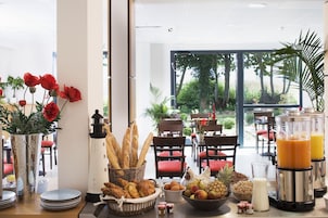 Buffet de café da manhã com pães, frutas e um dispensador de sucos.