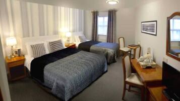 Quarto de hotel com duas camas, uma escrivaninha com cadeira, um abajur e um quadro na parede.
