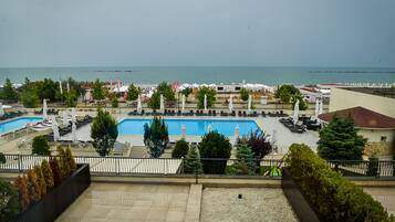 Área de piscina no terraço com várias piscinas, guarda-sóis e espreguiçadeiras, com vista para um corpo de água.