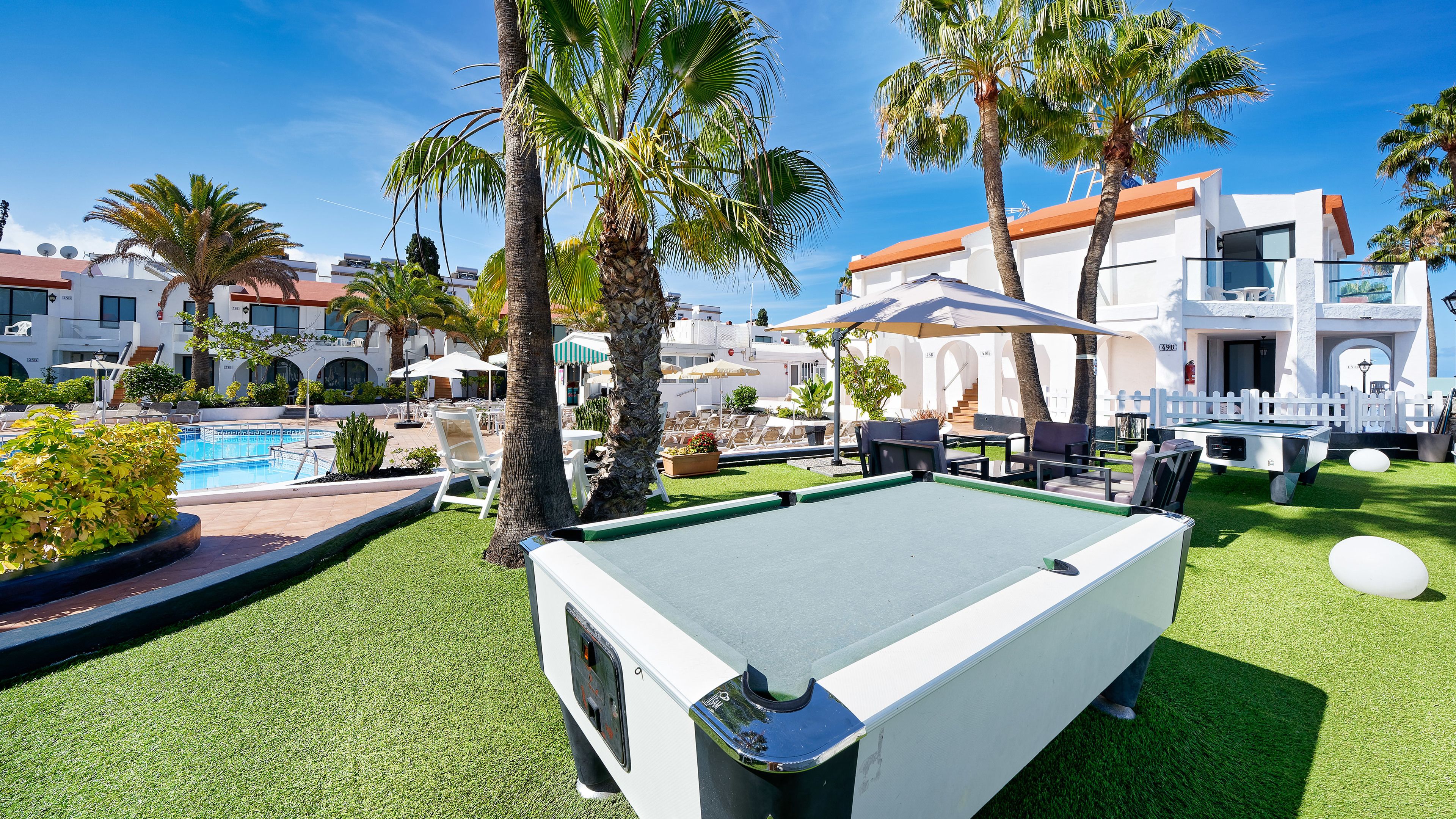 Uma área de piscina com mesa de bilhar, espreguiçadeiras e palmeiras.