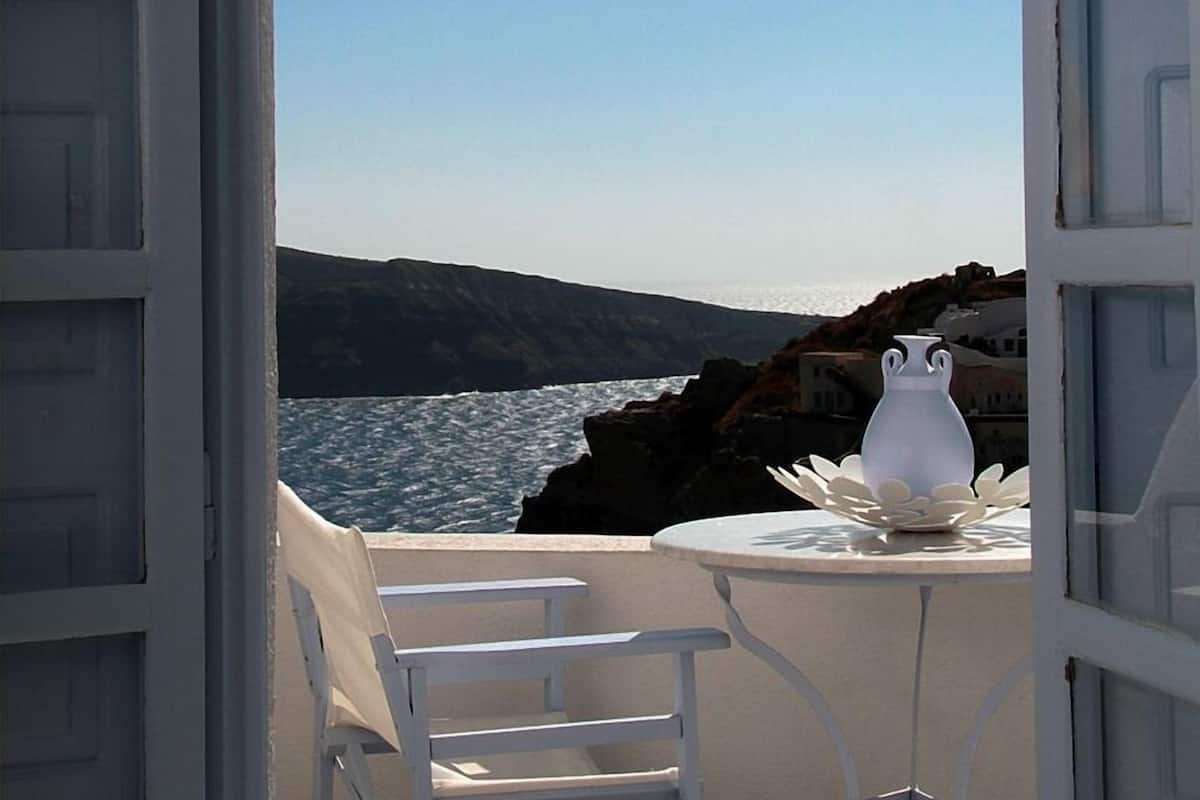 Varanda com cadeira branca e mesa, com vista para paisagem costeira com falésias rochosas e o mar.