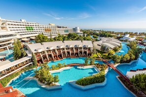 Um resort com várias piscinas, um edifício grande com varandas e vegetação exuberante.