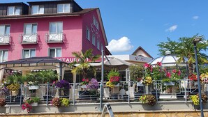 Um hotel com fachada rosa, área de estar externa com guarda-sóis e diversos vasos de plantas.