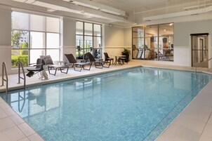 Uma piscina interior com água azul cristalina, rodeada por espreguiçadeiras e um solário.