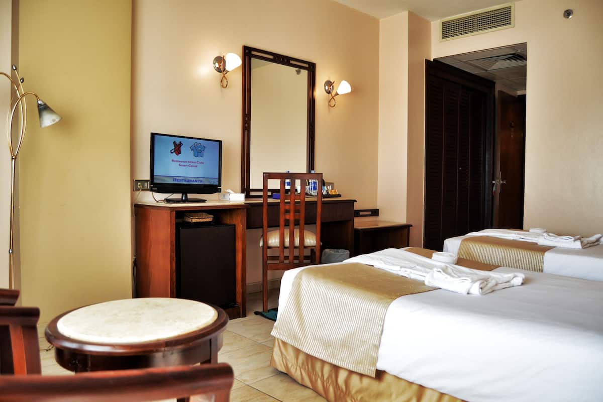 Quarto de hotel com duas camas, uma mesa de escritório com computador, uma cadeira e uma mesa redonda.