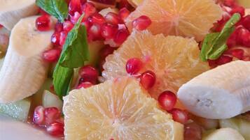 Salada de frutas com bananas, laranjas, sementes de romã e folhas de hortelã em um prato branco.