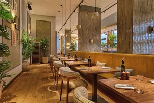 Um restaurante com mesas e cadeiras de madeira, plantas em vasos e uma grande janela.