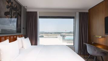 Quarto de hotel com uma cama grande, uma escrivaninha e vista para o aeroporto.