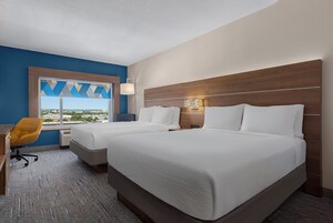 Quarto de hotel com duas camas, uma escrivaninha, uma cadeira e janela com vista.