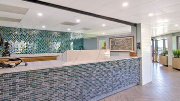 Uma área de recepção com balcão de mármore, parede em mosaico, obras de arte emolduradas e plantas.