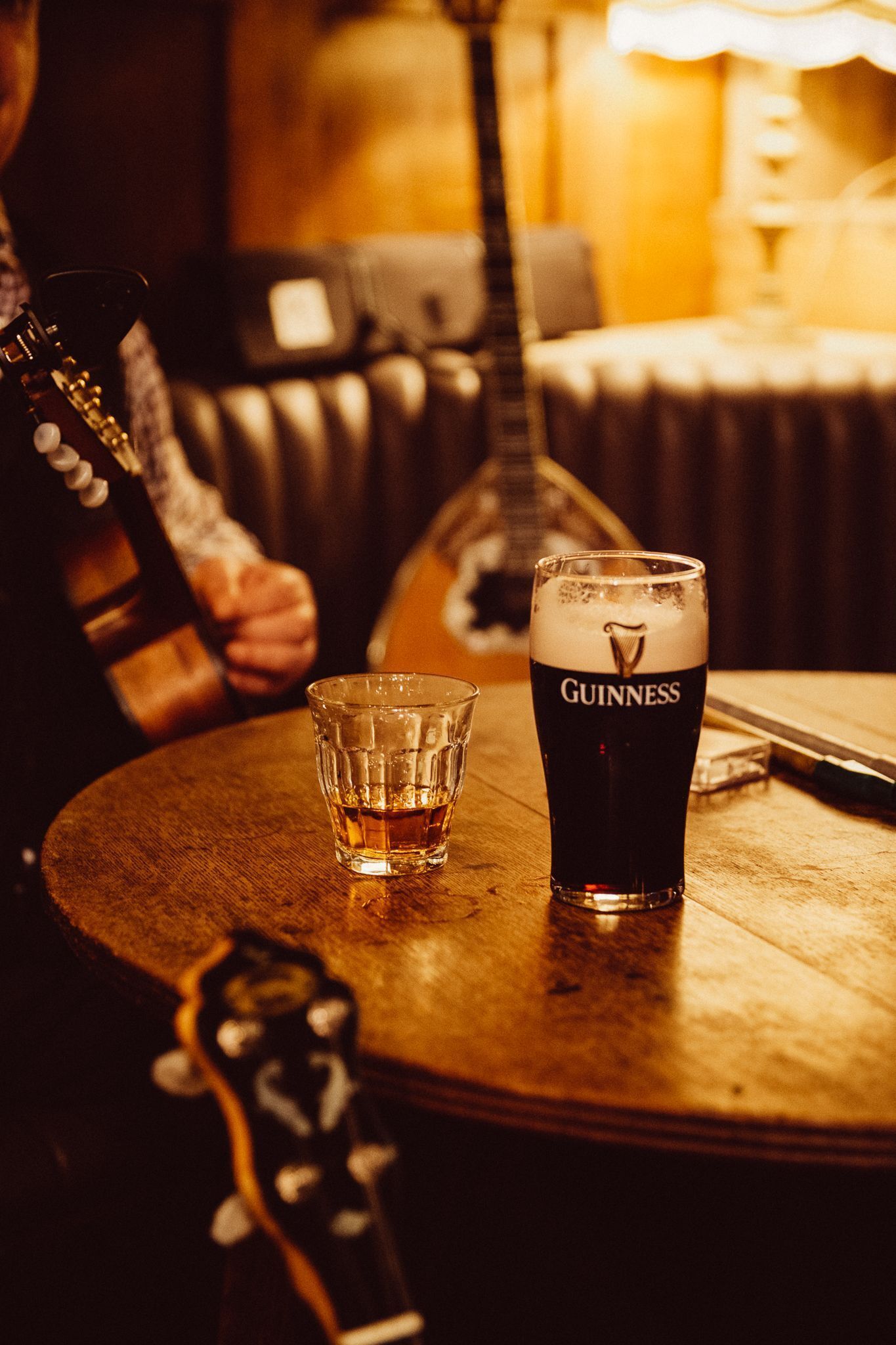 Um copo de cerveja Guinness sobre uma mesa de madeira, com um violão ao fundo.