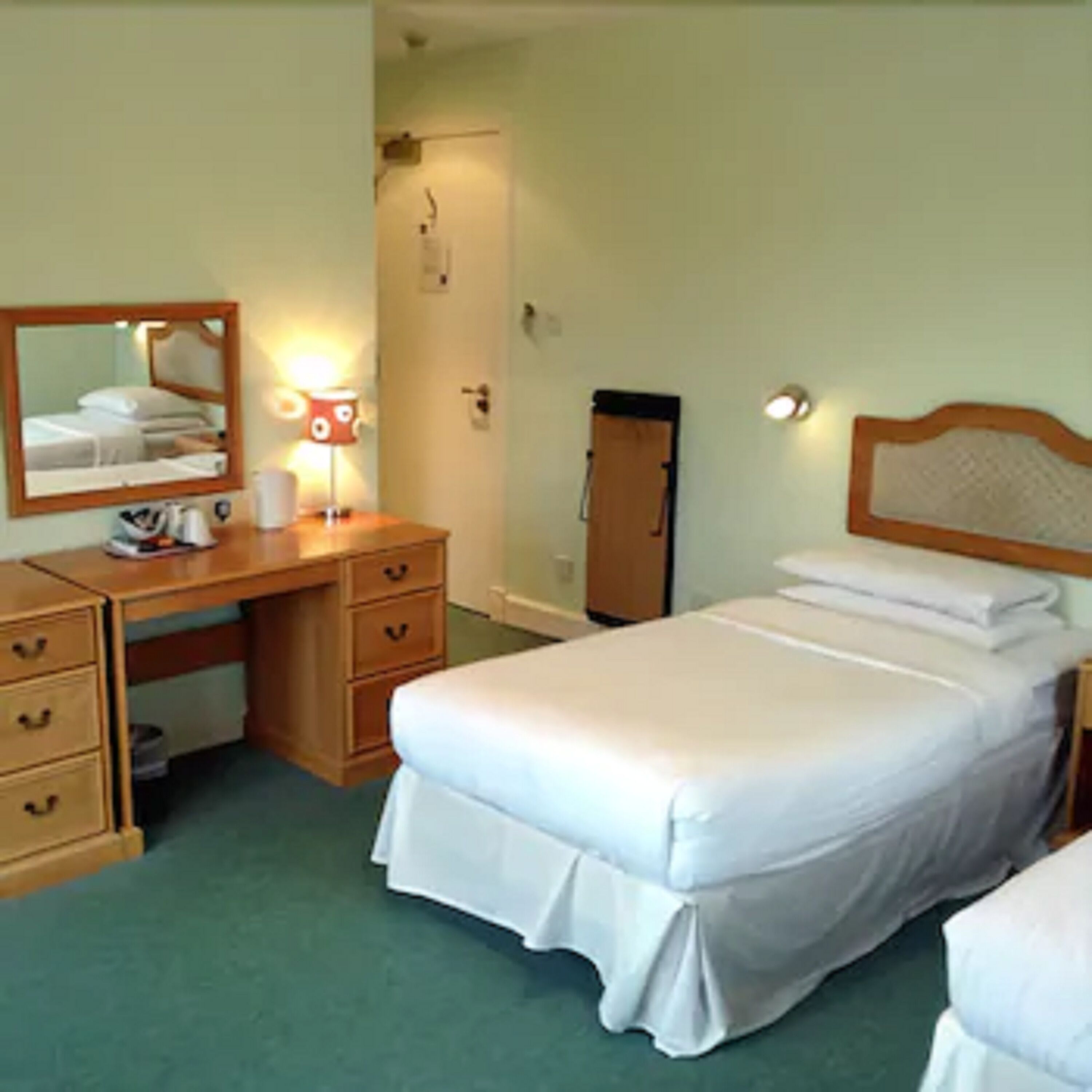 Quarto de hotel com cama, escrivaninha, espelho e guarda-roupa.