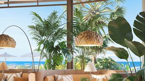 Uma área de estar ao ar livre aconchegante com vista para o oceano, com móveis de madeira, plantas em vasos e luminárias pendentes.