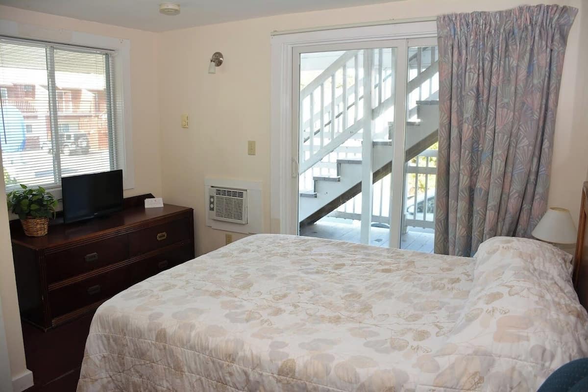 Quarto com cama, cômoda, televisão, aparelho de ar condicionado e vista para uma escada que dá para o exterior.