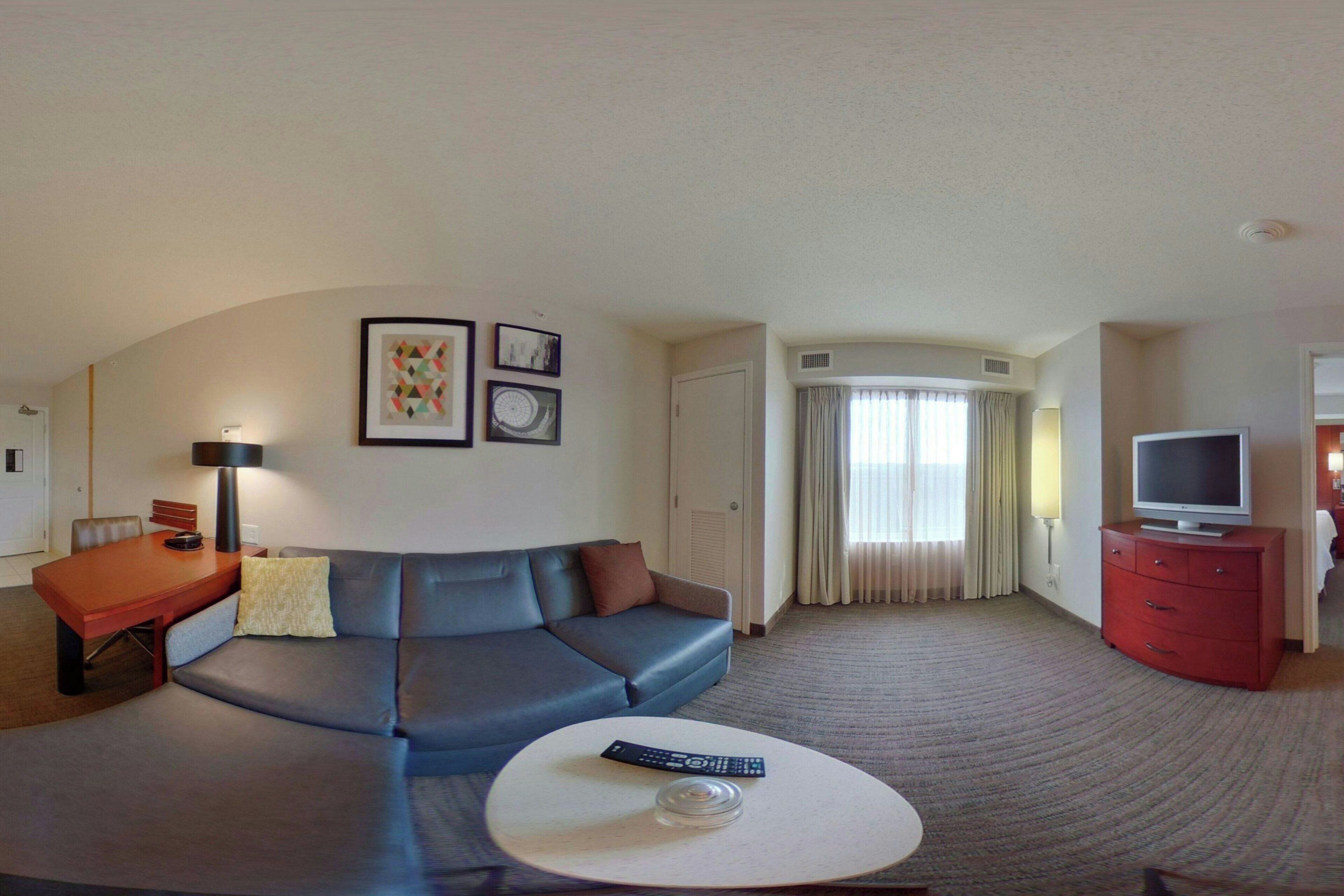 Quarto de hotel com sofá, uma pequena mesa, televisão e cómoda vermelha.