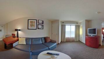 Quarto de hotel com sofá, uma pequena mesa, televisão e cómoda vermelha.