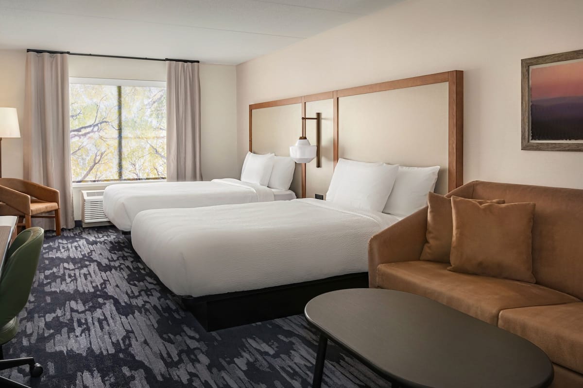 Quarto de hotel com duas camas, um sofá, uma mesa e uma janela com cortinas.