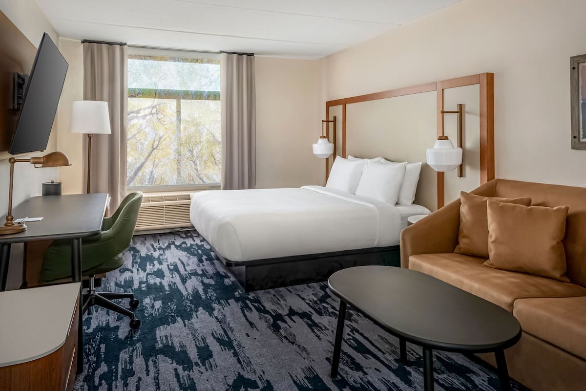 Quarto de hotel com cama, sofá, escrivaninha com cadeira, televisão e janela com cortinas.