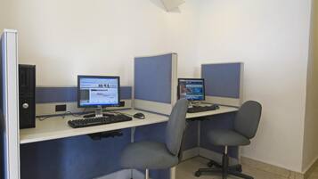 Espaço de escritório de hotel com duas estações de trabalho, cada uma com monitor, teclado e rato.