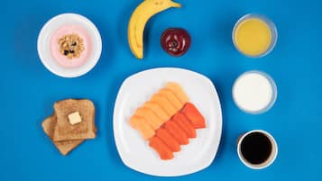 Mesa de café da manhã com torradas, banana, maçã, iogurte, suco de laranja, leite e café.