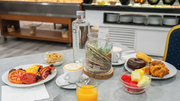 Um buffet de café da manhã com diversos alimentos, um copo de suco de laranja e uma xícara de café.