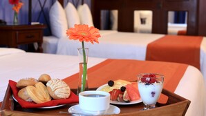 Quarto de hotel com uma bandeja de café da manhã bem arrumada, incluindo pães, frutas, iogurte e café.